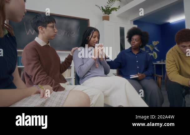 Medium wide shot of crying Black teen girl surrounded by empathic young ...