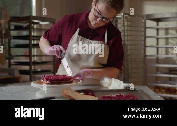 Medium shot of Caucasian female baker in maroon shirt and apron ...