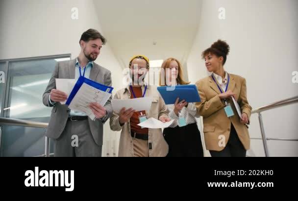 Diverse businesspeople walk holding documents on office corridor bridge ...