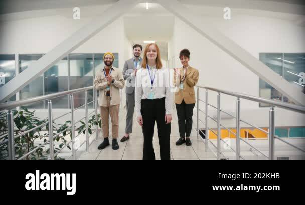 Red-haired young businesswoman crosses arms while employees stand behind in office corridor ...