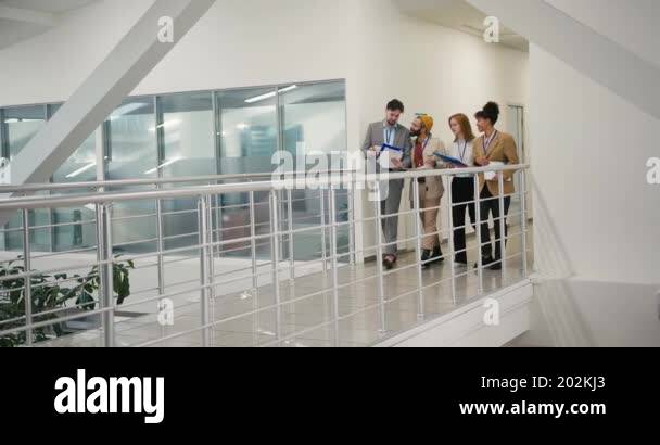 Diverse businesspeople walk holding documents on office corridor bridge ...