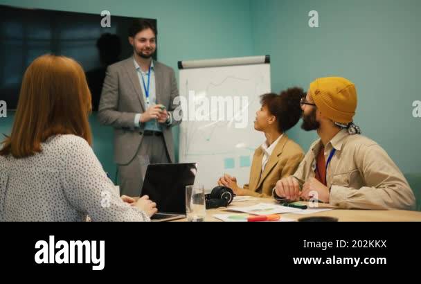 Cheerful bearded man speaker stands at whiteboard while workers clap ...