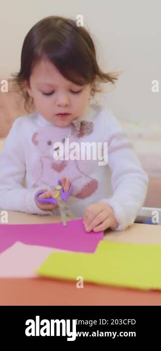 little child girl cuts colored paper with scissors at the table. kids ...