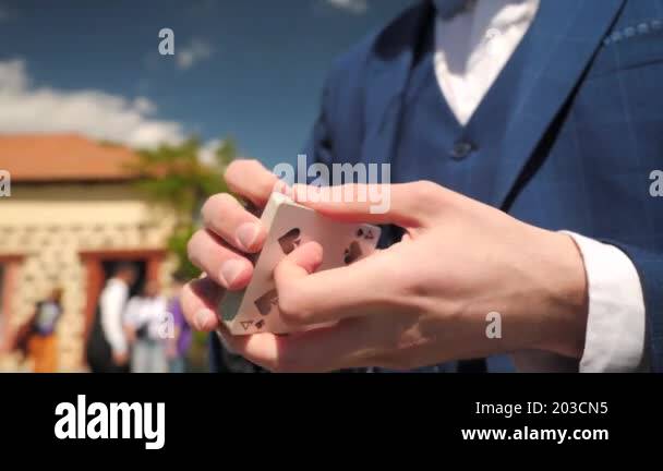 A magician wearing a blue suit is performing a card trick outside ...