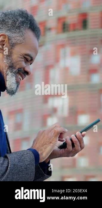 Vertical video of happy senior black man using mobile phone in ...