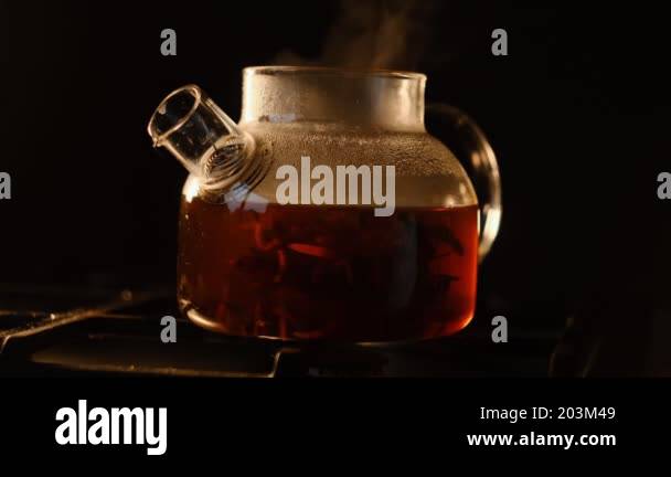 Slow motion of tea leaves swirling in water inside glass teapot ...