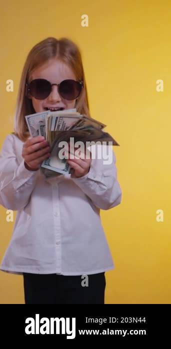 Vertical, a confident smiling child holds money dollars in her hands ...