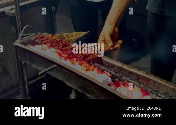 A detailed view of a sizzling satay grill as the vendor expertly cooks ...