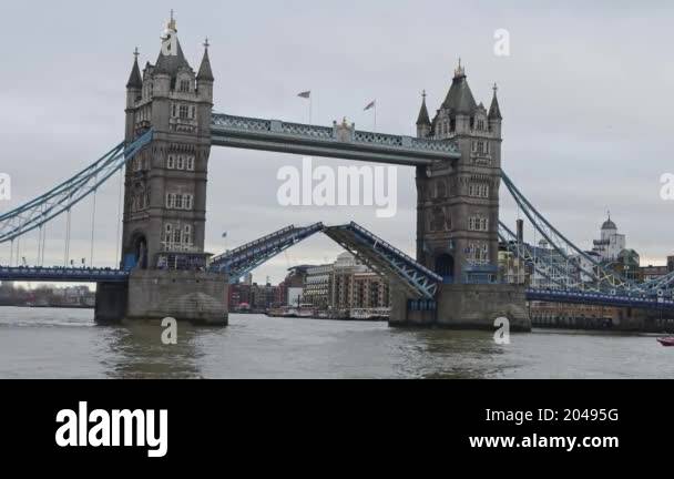 Tower Bridge's bascules are raised for a boat, set against an overcast ...