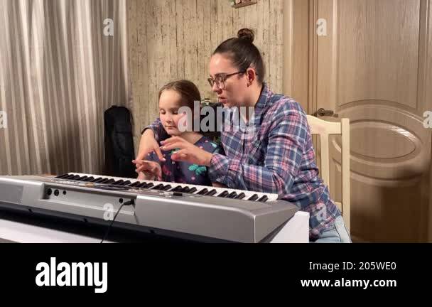 A young music teacher guides a child in learning to play the digital ...