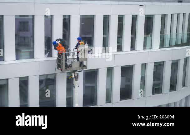 Two workers wearing safety harness wash walls, panels and windows of ...