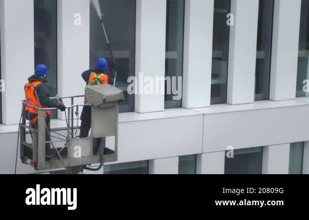 Two workers wearing safety harness wash walls, panels and windows of ...