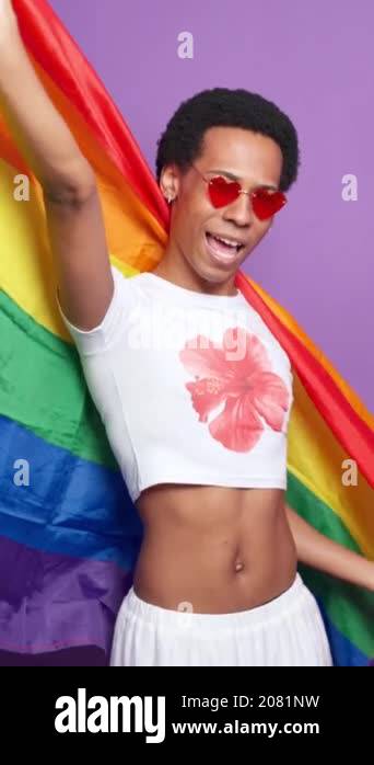 Young man with red heart-shaped sunglasses dancing with rainbow flag ...