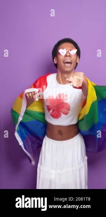 Joyful non-binary activist dancing with rainbow flag against purple ...