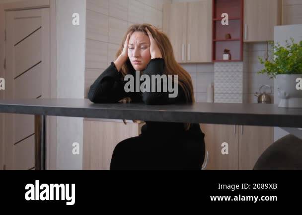 Young woman sits at her kitchen counter, struggling with intense ...