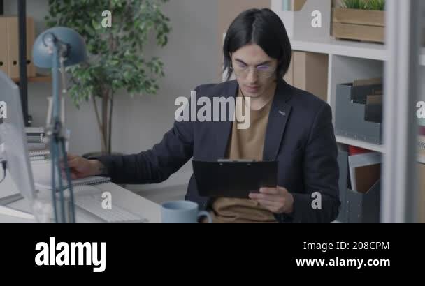 Asian businessman studying documents looking at computer screen writing ...