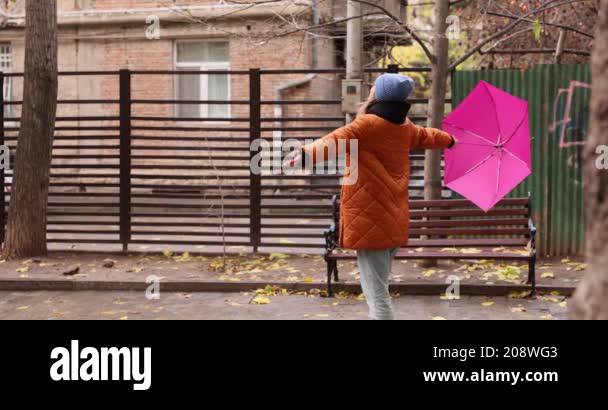 A spirited woman joyfully dances outdoors under the sunlight, twirling with a pink umbrella amid ...