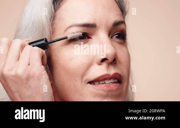 Closeup of a senior woman using mascara on her eyelashes, emphasizing a ...