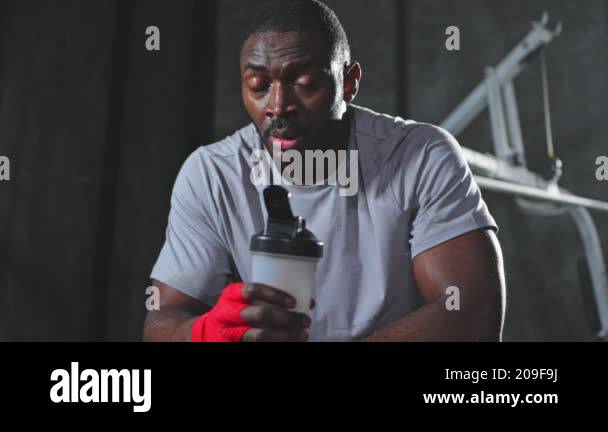 Boxer in gym. Tired African man fighter with red boxing wraps resting ...
