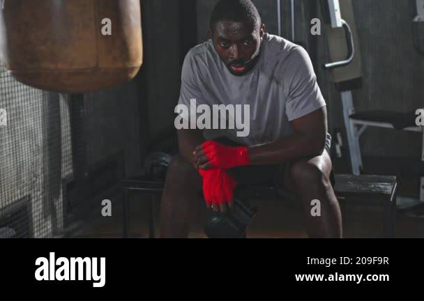 Boxer in gym. Tired African man fighter with red boxing wraps resting ...
