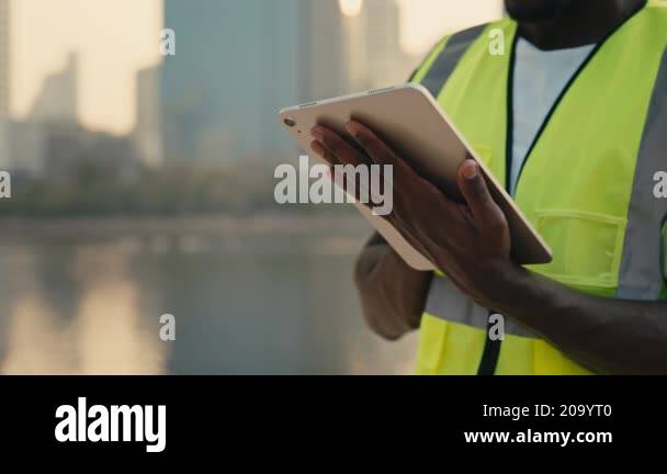 African American technician holds tablet computer standing on city ...