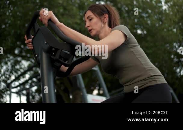 Pretty woman training legs on cross trainer using outdoor gym equipment ...