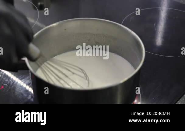 whisking a creamy white sauce in a stainless steel saucepan on a ...