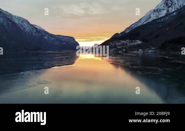 A glowing golden winter sunset reflects on a frozen fjord in Norway ...