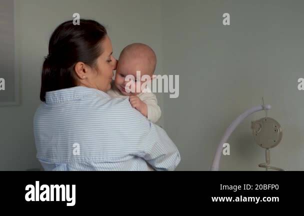 Loving mom tenderly holding her newborn baby at home. Close up portrait of happy mother holding ...