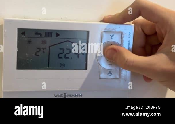 A hand skillfully adjusts a sleek, modern thermostat that displays the ...