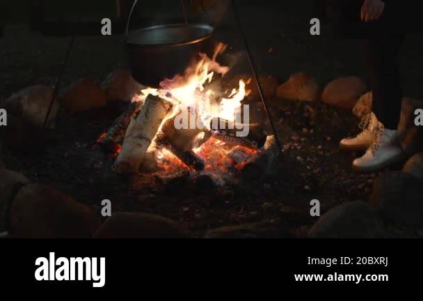 A fire, a pot hanging on it, in which food is being cooked, the hostess ...