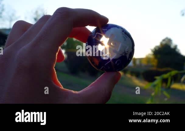 Hand rotating a 3D globe puzzle, capturing sun rays in missing piece ...