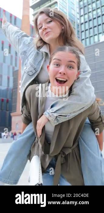 Vertical. Cheerful young woman giving her friend a piggyback ride while ...
