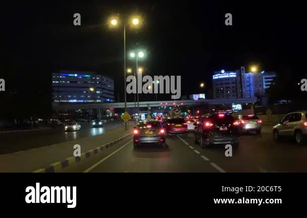 A bustling urban scene at night, showcasing a lineup of cars in a traffic jam, illuminated by ...
