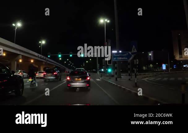 Night time urban scene at a traffic light intersection. Multiple cars are visible, with several ...