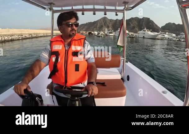 Close-shot of man in an orange life jacket steering a small boat ...