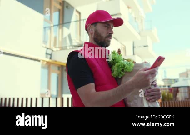 Portrait of young courier man use phone looking for a house holding ...