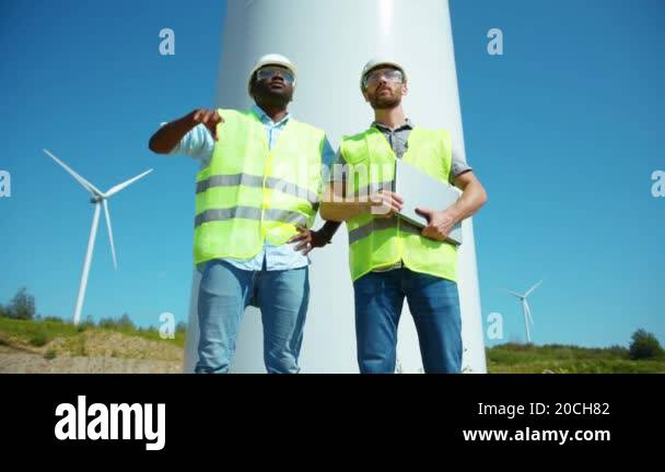 Two workers men in uniform discuss the wind turbines stand ecological ...