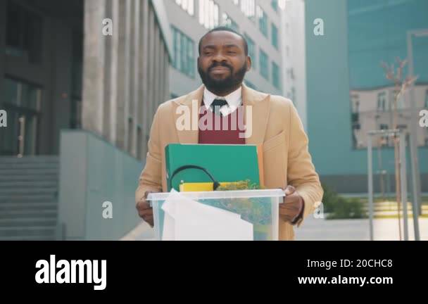 Upset african american office worker man walking with box of personal ...