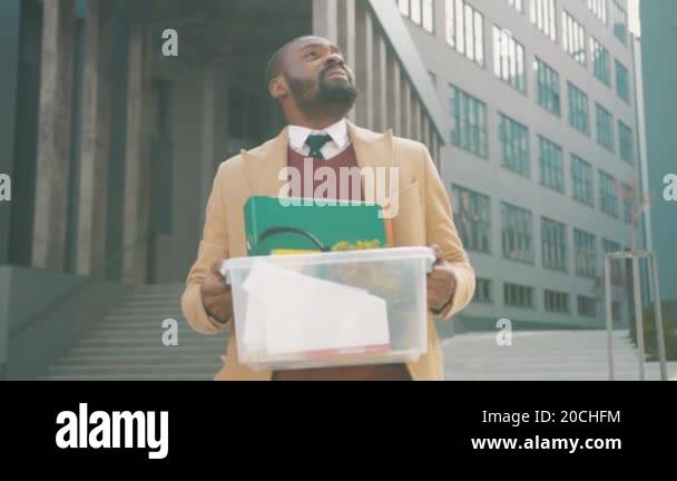 Depressed african american office worker man walking with box of ...