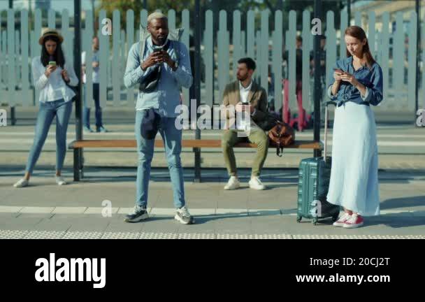On bus stop mixed-races young males and females people standing keeping ...