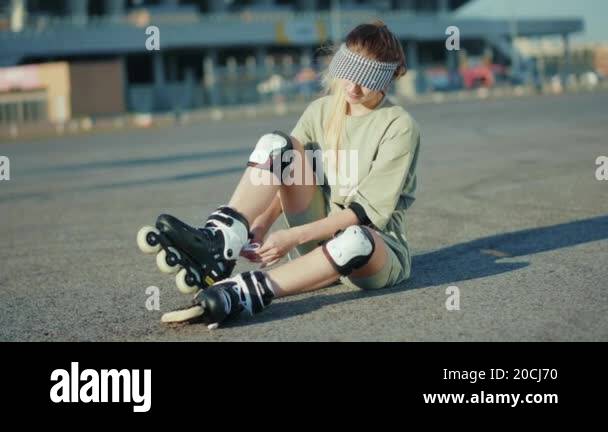 Slow motion young woman sitting on ground and putting roller skates ...