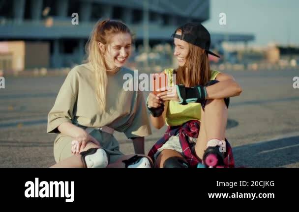 Close up young women sitting on ground with roller skates use phone ...