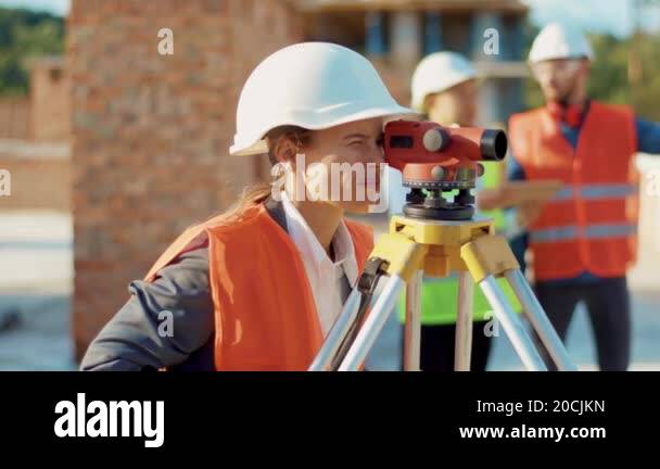 Close up young woman surveyor in work clothes and helmet takes measures ...