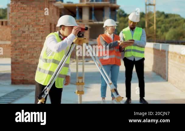 Asian man engineer surveyor takes measures with theodolite stand helmet hardhat geodesy building ...