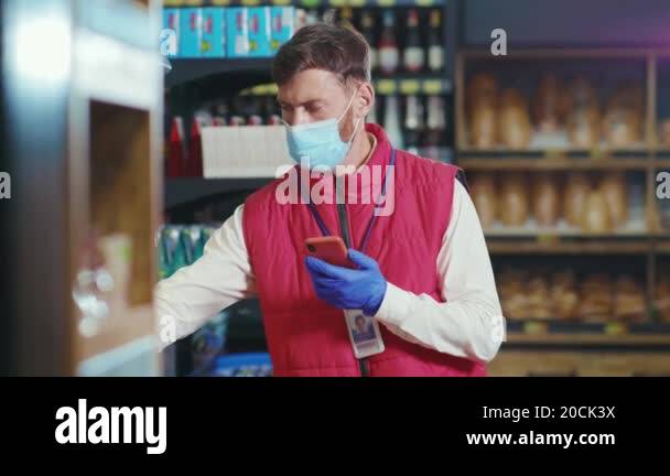 Young seller man with mask use phone in supermarket hold avocado in ...