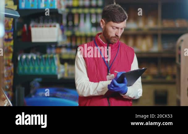 Portrait young seller man write in notebook in supermarket look camera ...