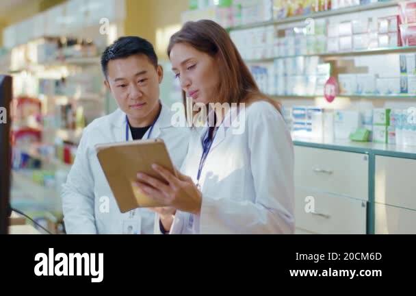 Asian adult and younger female intern cooperating in drugstore. Aspiring woman apothecarist ...