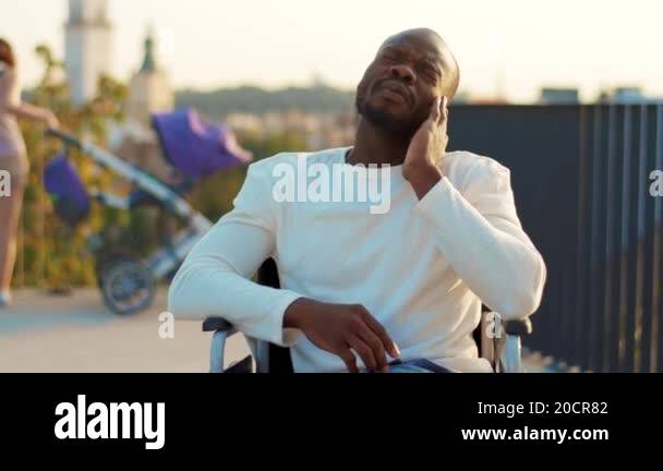 Close up young man use headphones speaking phone on a wheelchair in a ...