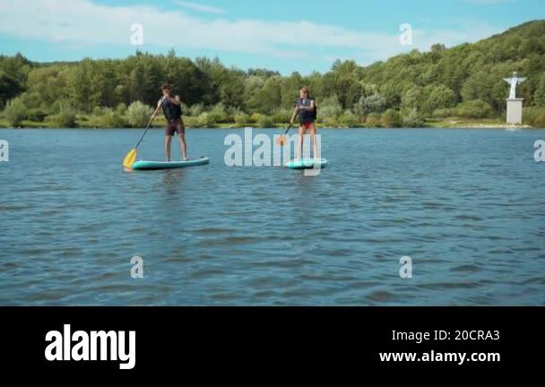 Happy young man and woman standing on sup board and swims surfing on ...